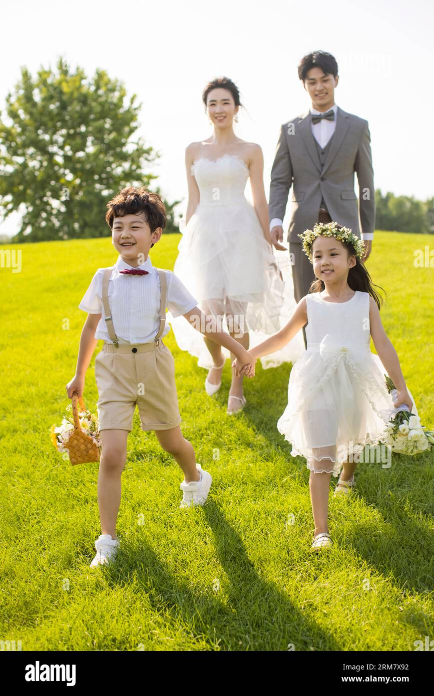 Chinese bride and groom walking through a park with flower girl and ...