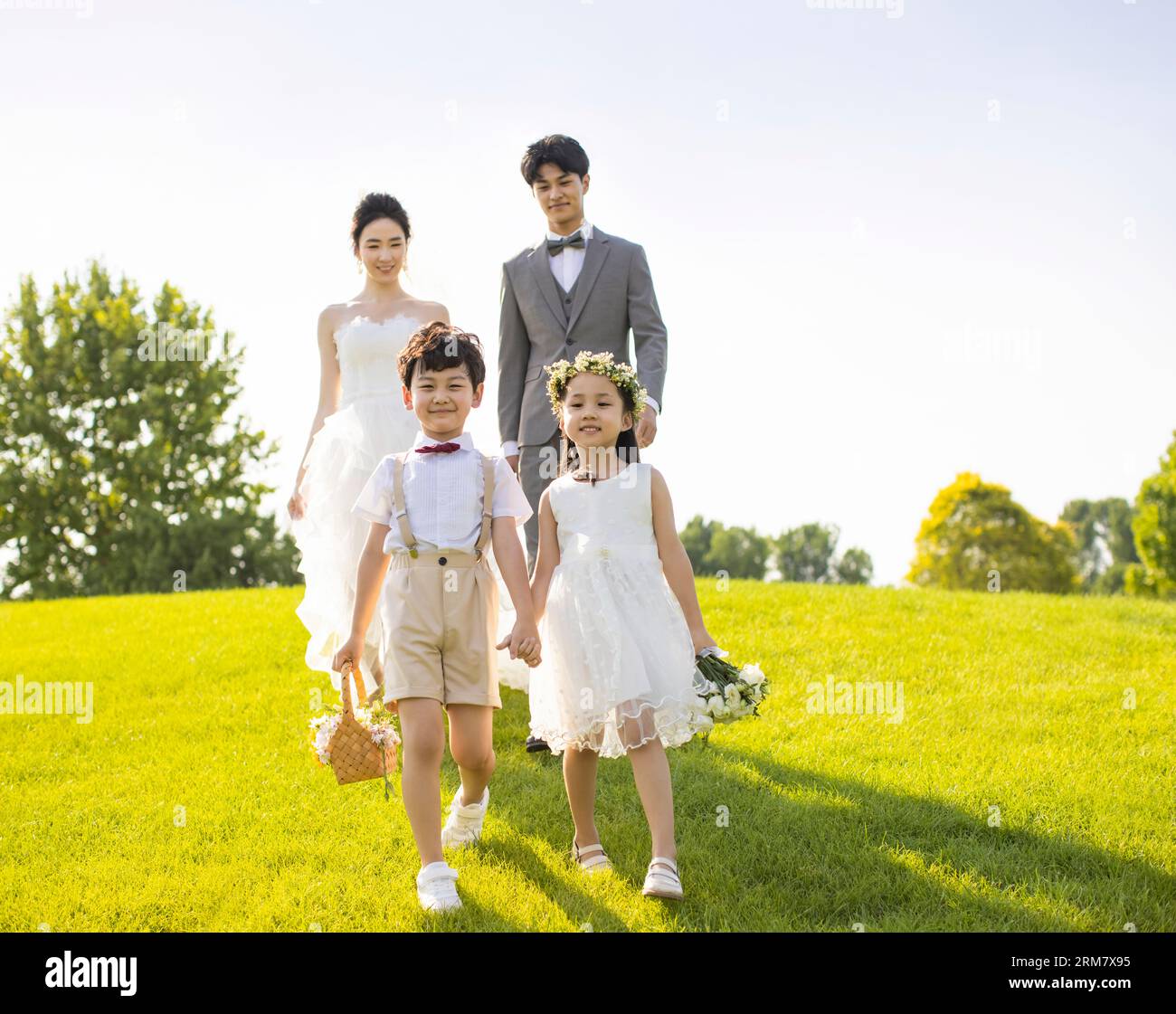 Chinese bride and groom walking through a park with flower girl and ...