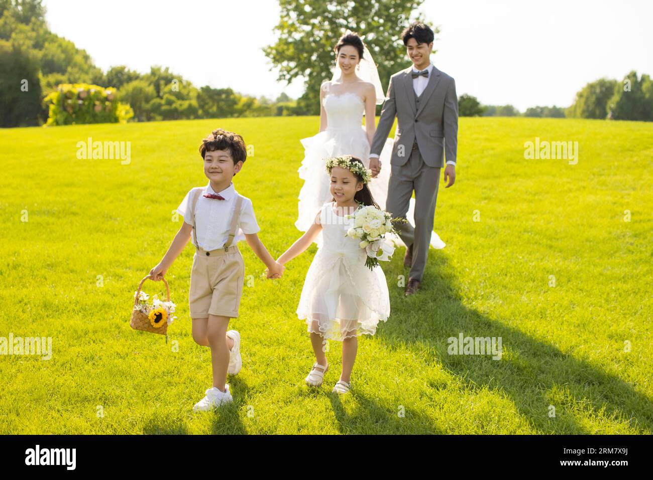 Chinese bride and groom walking through a park with flower girl and ...