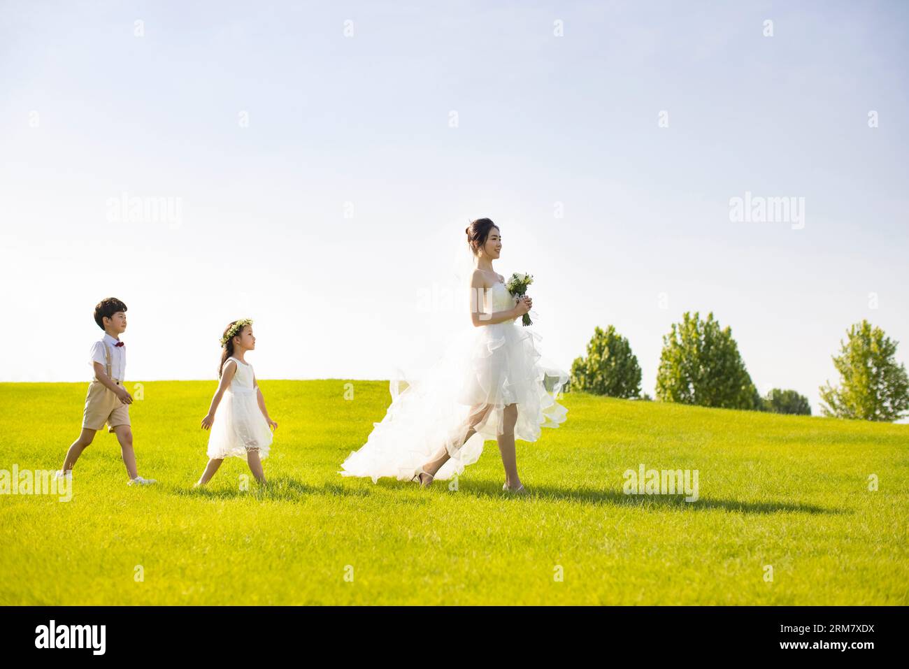 Beautiful Chinese bride walking through a park with flower girl and ...
