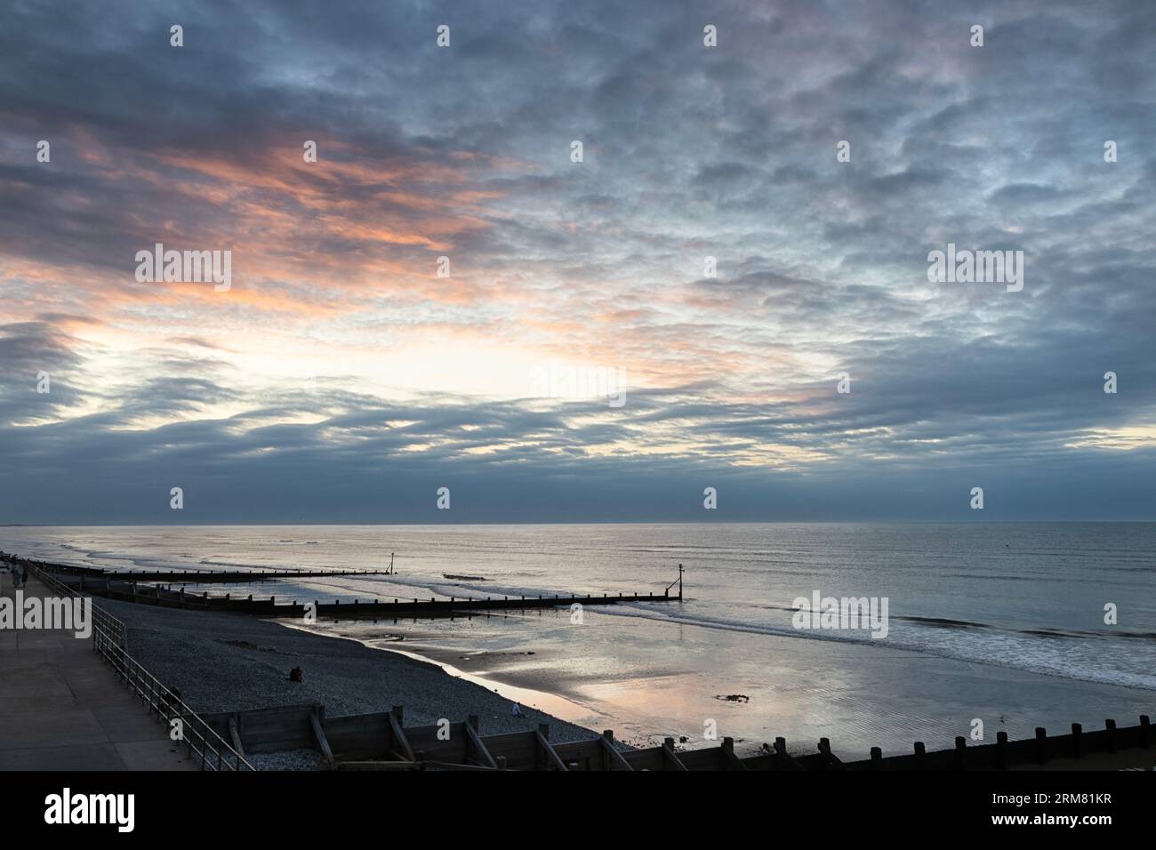 Cloudy sunset over Sheringham breach, peaceful walkers on the shore ...