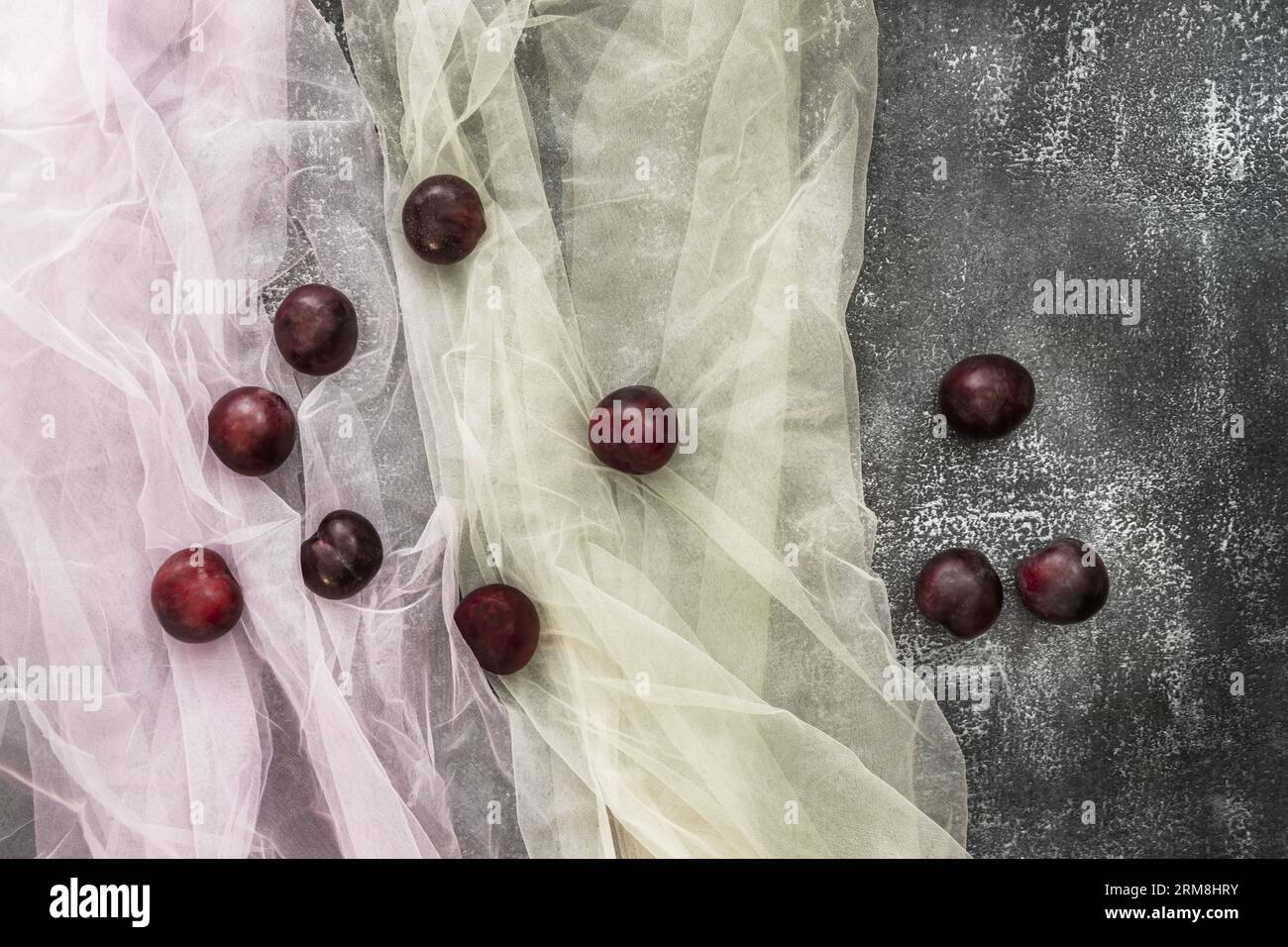 A few red plums on a semi-transparent cloth of various colors and a ...