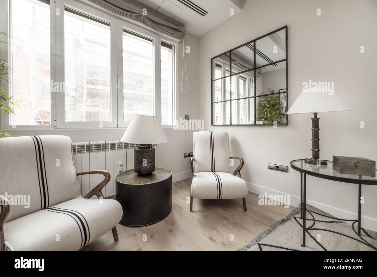 Living room corner with white single sofas, mirror on the wall, side ...