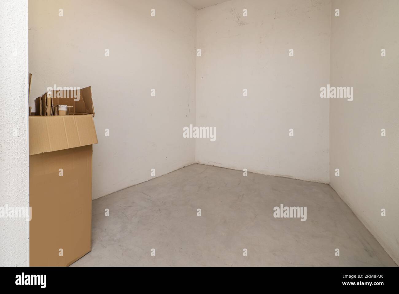 A small empty storage room with a cardboard box and raw concrete floors ...