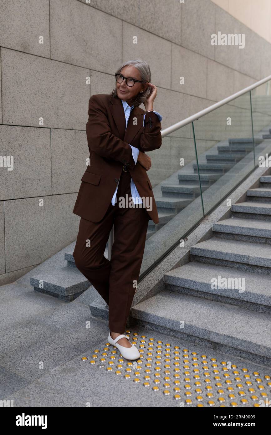 charming successful senior woman with gray hair and glasses is dressed ...