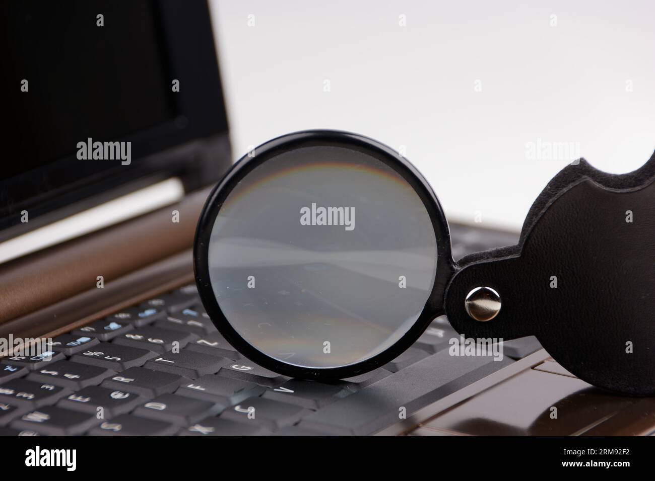 Laptop computer with keyboard and magnifying glass on top, representing ...