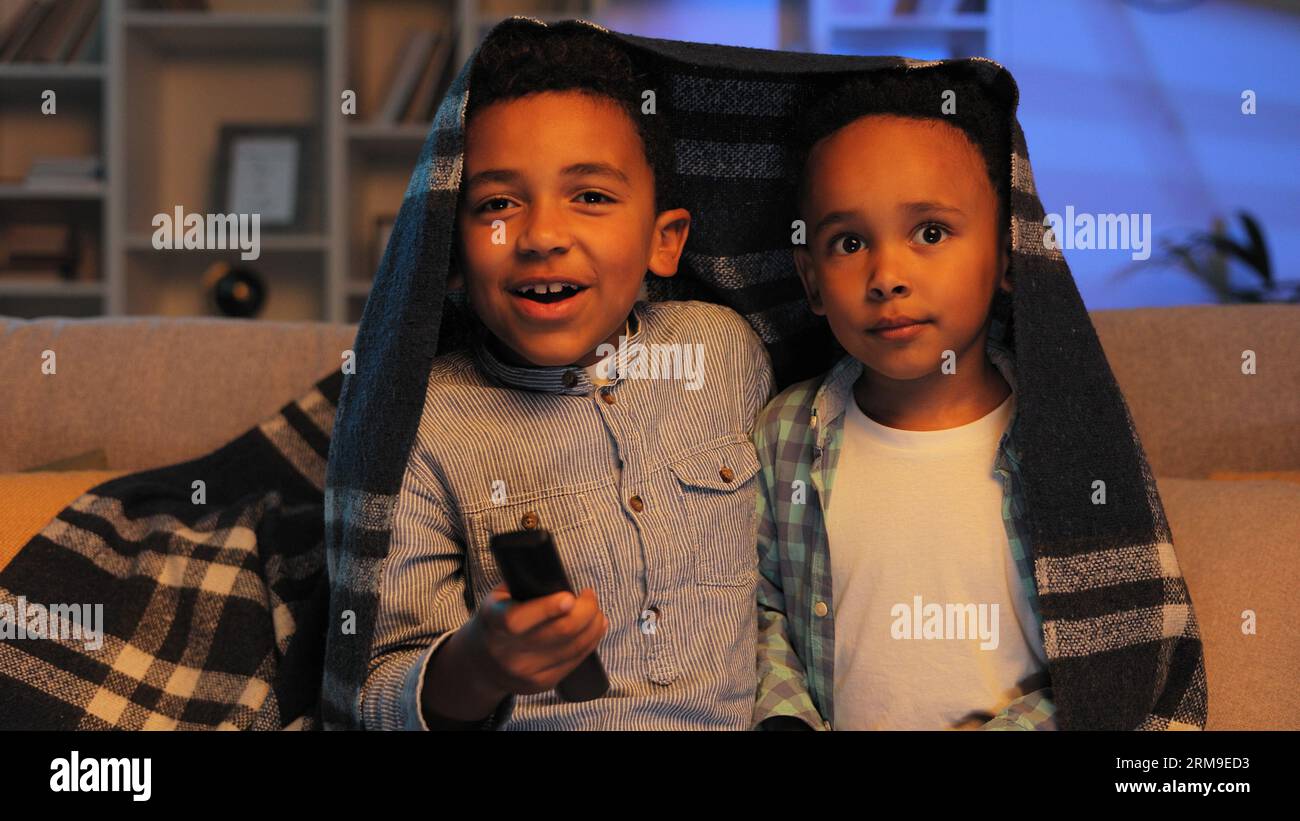 Two little African American brothers are sitting on the sofa covered ...