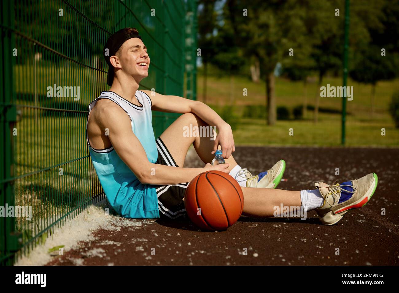 Satisfied teenage basketball player rest sitting on street court Stock ...