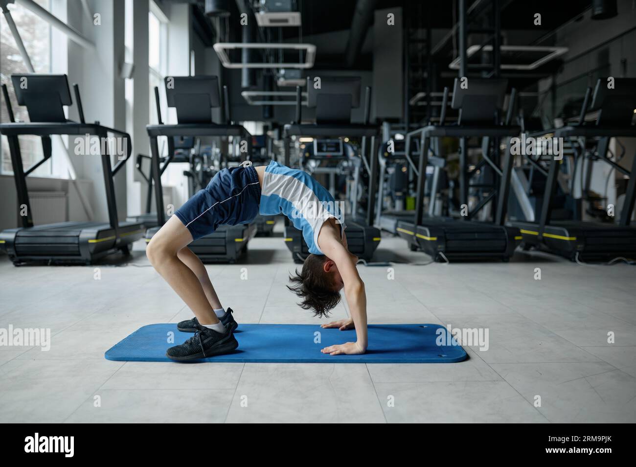 Teenager boy doing gymnastics exercise standing in bridge position ...
