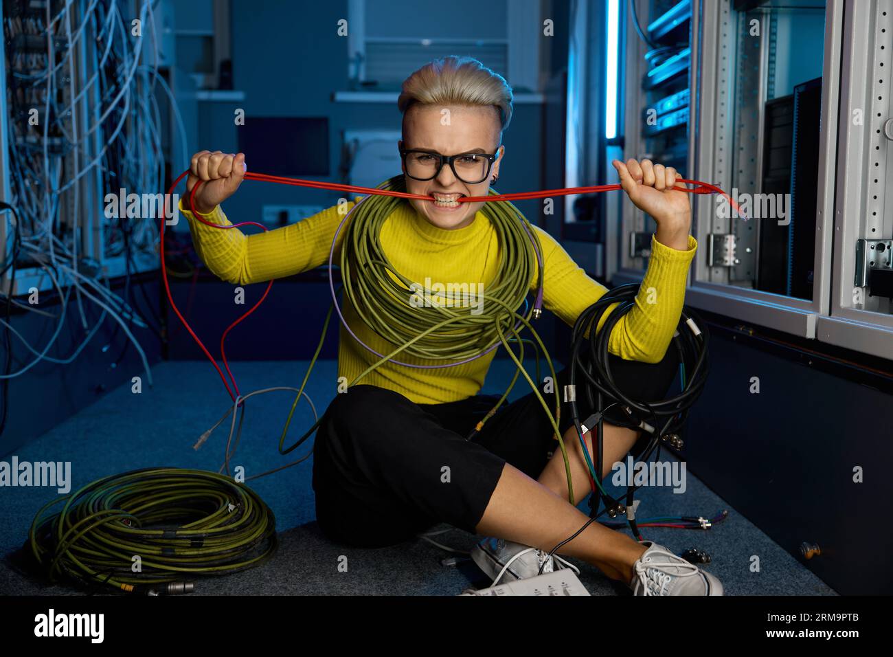 Angry woman maintenance worker biting wire while sitting in server room ...