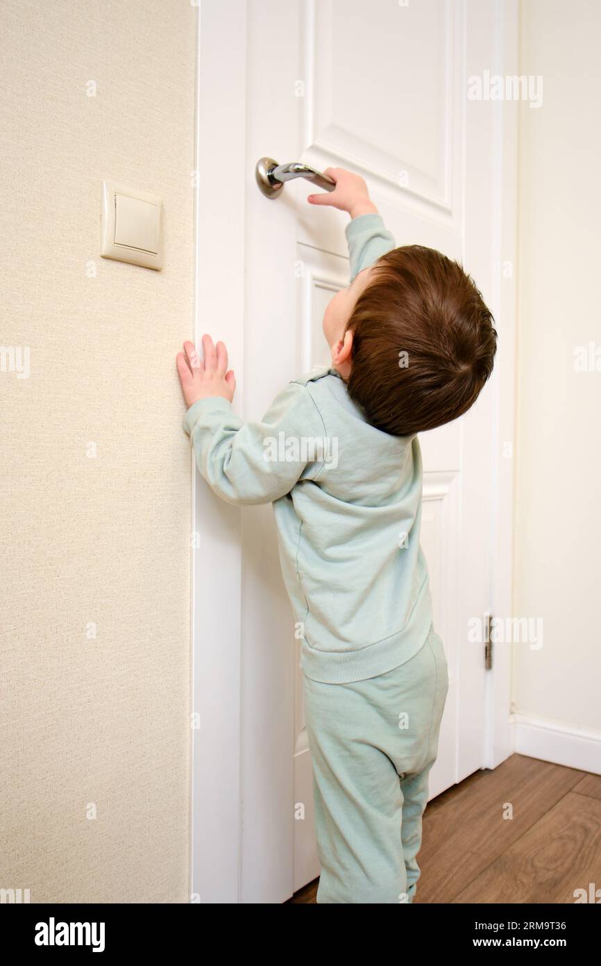 Little baby opens the door. Child pulls the door handle with the lock ...