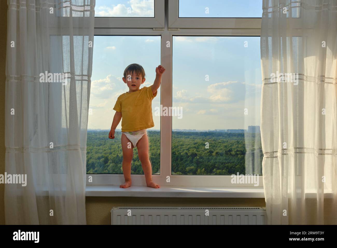 Baby boy is standing on the high window sill, risking their safety. Kid ...