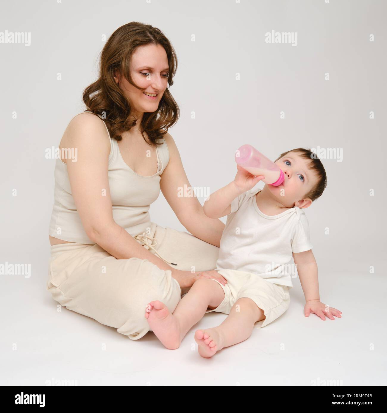 Happy baby with mother drinks milk from bottle on studio white ...