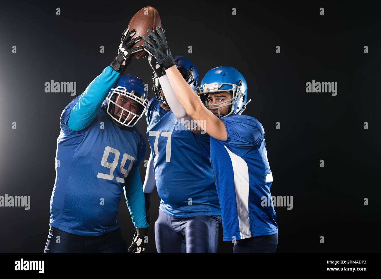 Three American football players raising their hands up holding the ball ...