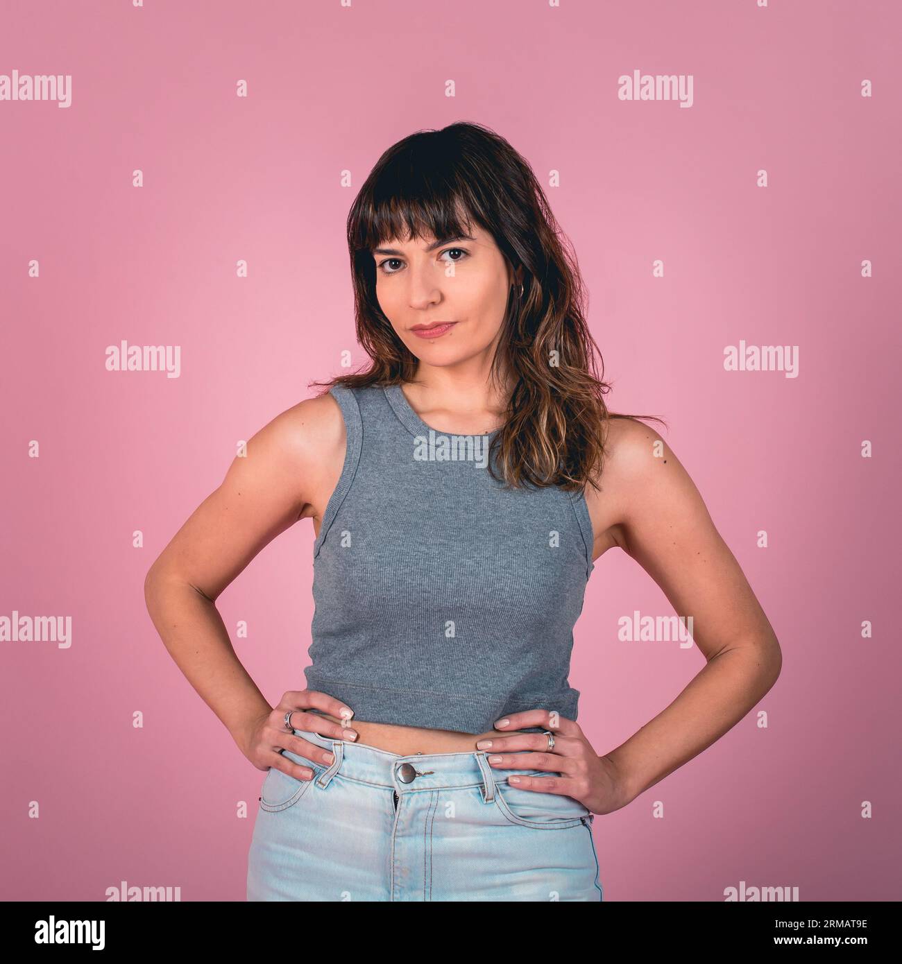 Studio portrait of a confidence woman with hands on hips while looking at camera over a pink ...