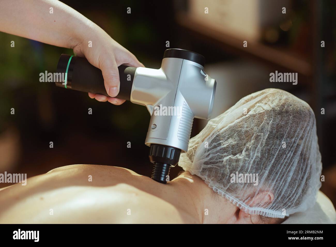 Healthcare time. Closeup on medical massage therapist in spa salon with massage pistol massaging ...