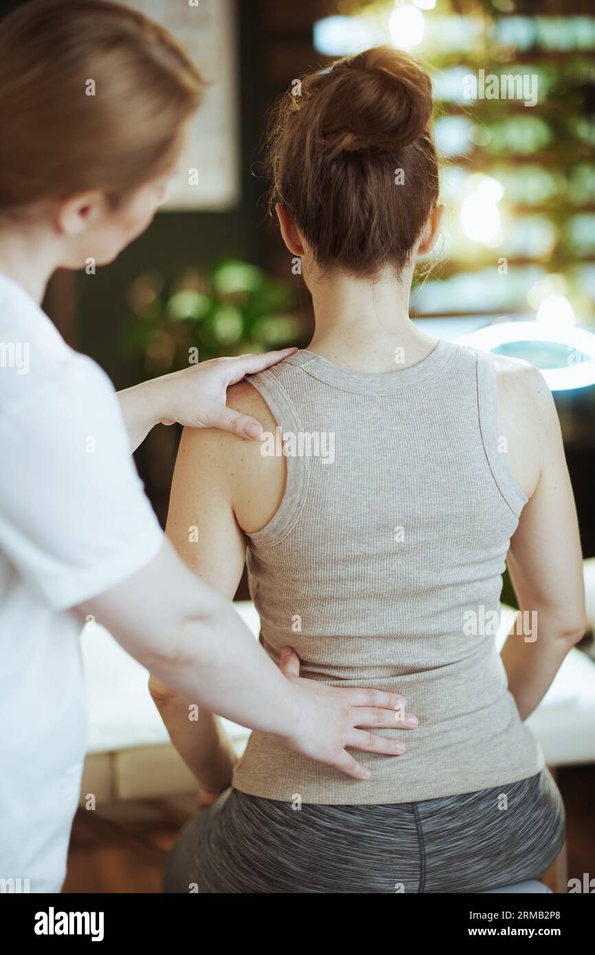 Healthcare time. Seen from behind massage therapist in massage cabinet checking clients back ...