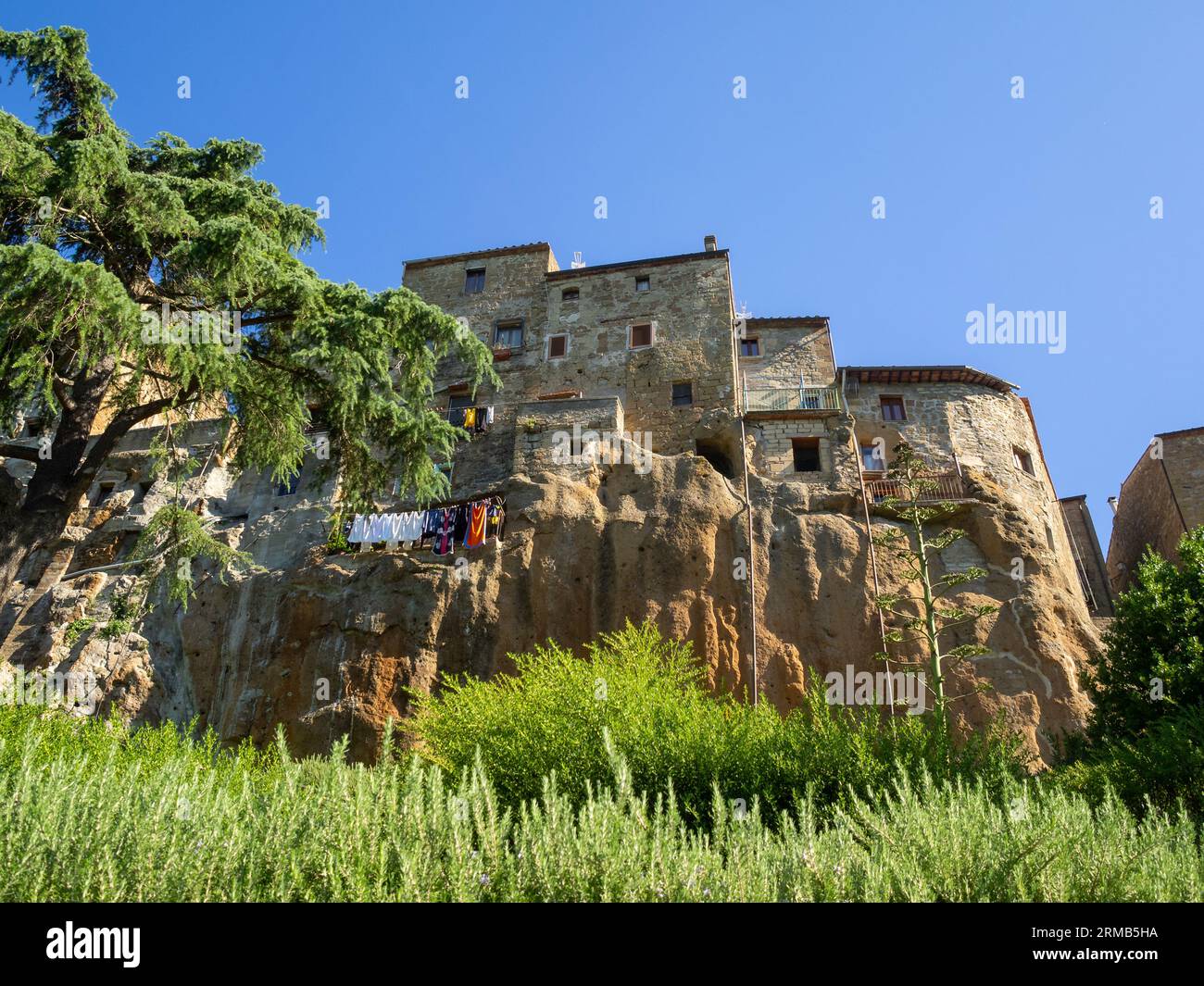 Looking up at Pitigliano stone buildings atop the rock cliff Stock ...
