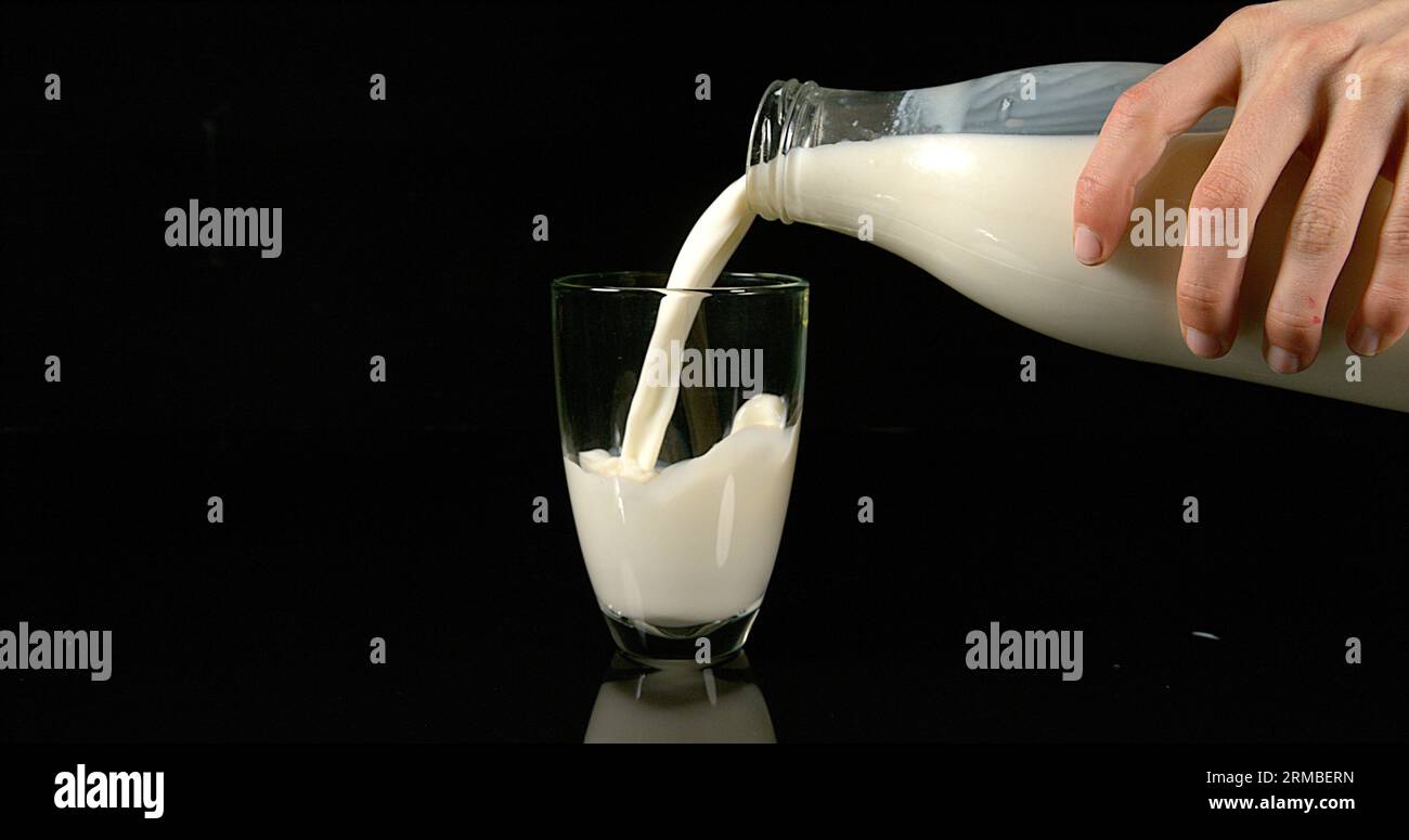 Milk being poured into Glass against black Background Stock Photo - Alamy