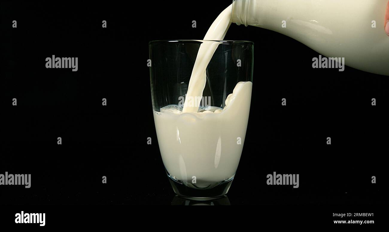 Milk being poured into Glass against black Background Stock Photo - Alamy