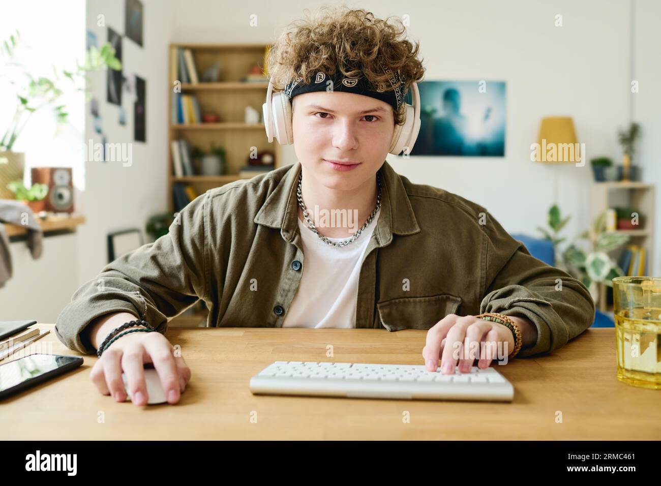 Cute teenage guy keeping hands on mouse and keyboard buttons while ...
