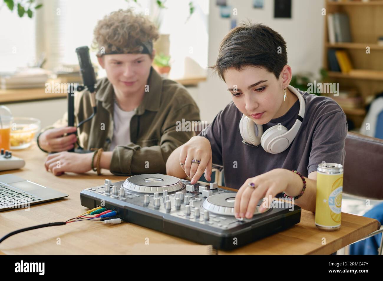 Cute teenage girl with headphones on neck adjusting turntables while ...