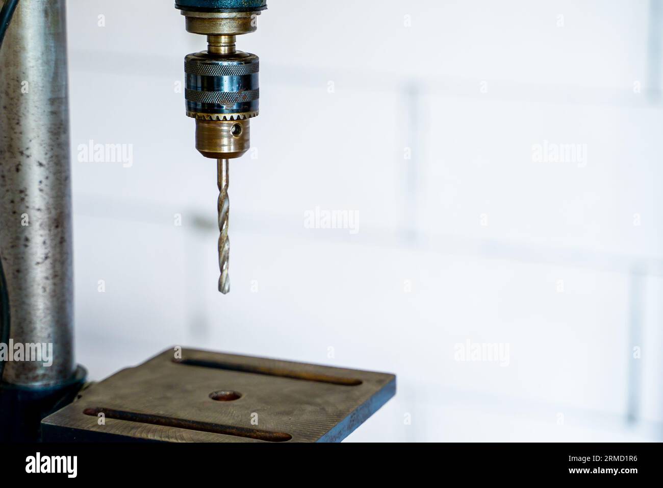 Old drilling machine with a metal drill close-up on a blurred light ...