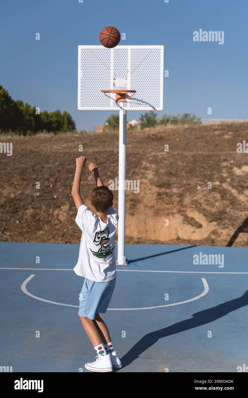 Young boy throwing ball into the hoop while playing basketball on an ...