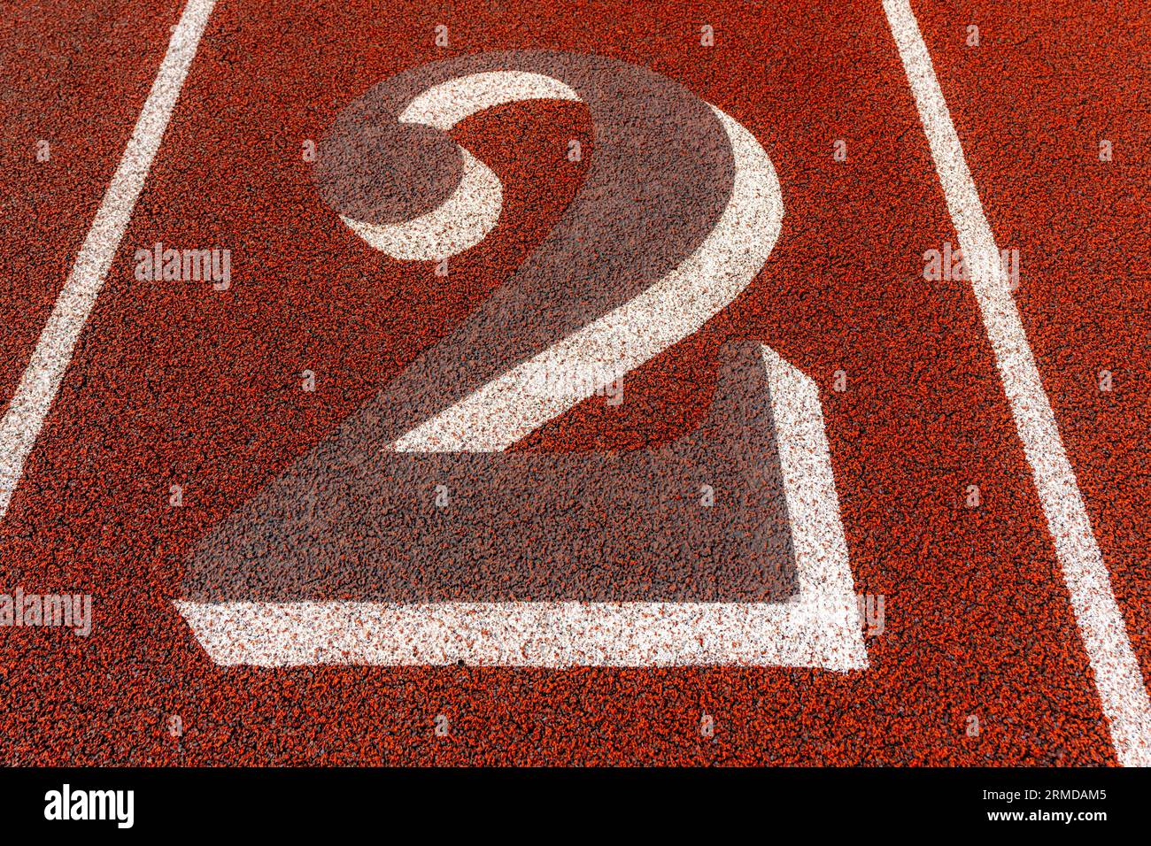 Close up lane number two 2 on a old red running track with white lane ...