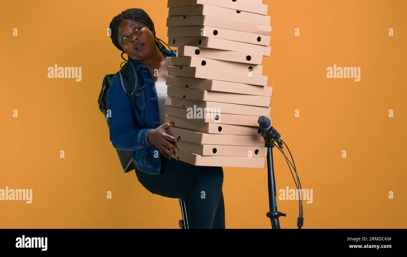 Youthful black woman holding stack of pizza boxes for delivering to a ...