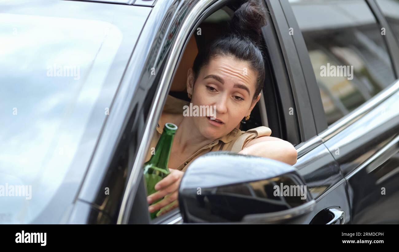 Drunk brunette woman driver holds alcohol bottle sitting in car Stock ...