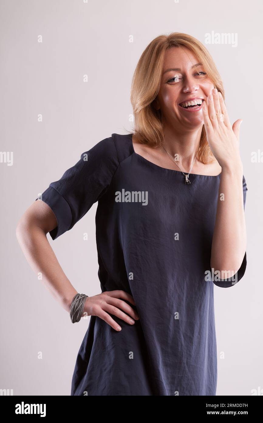 Blonde woman in a gray-blue dress makes a playful gesture as if to hide ...