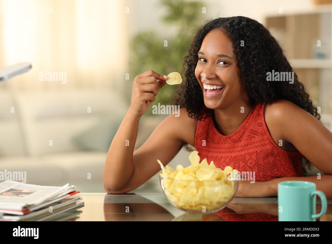 Happy black woman eating potato chips looking at you at home Stock ...