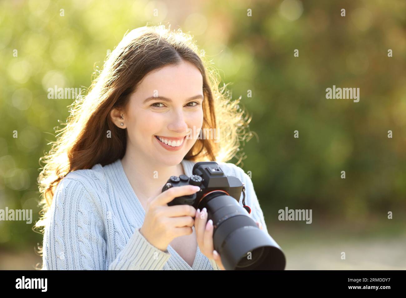 Happy photographer posing in a park holding mirrorless camera looking ...
