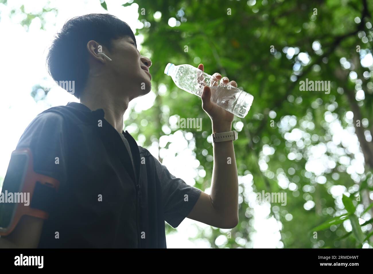 Happy asian male runner drinking water from a bottle, resting after ...