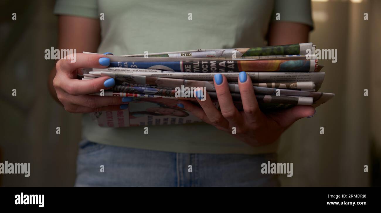 A woman stacks old newspapers in a pile, waste paper collect. Preparing ...