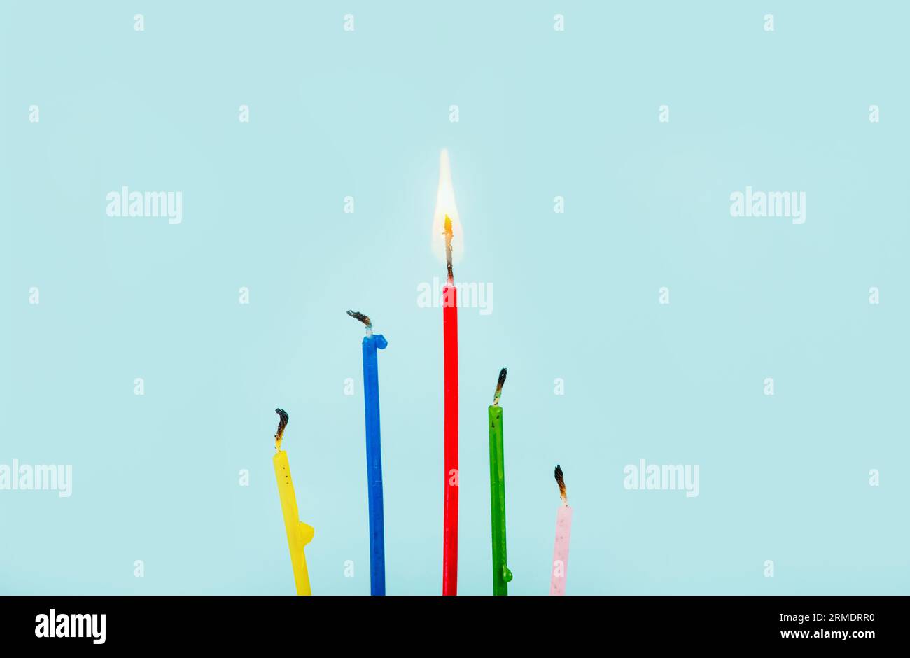 One candle burning and others are put out on blue background with lot ...