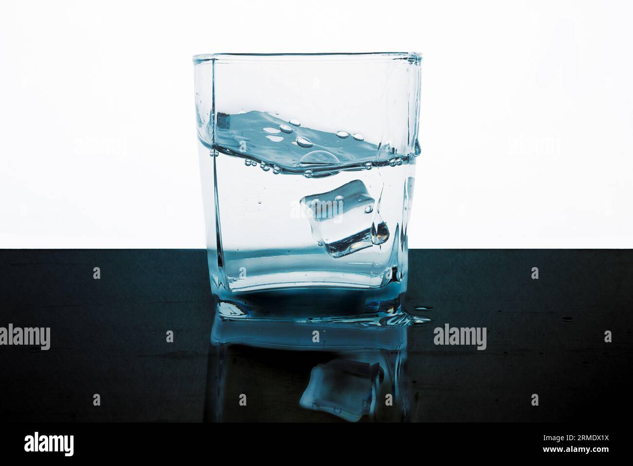 One ice cube dropped into a glass of water. Black and white background. Turbulent water in the ...