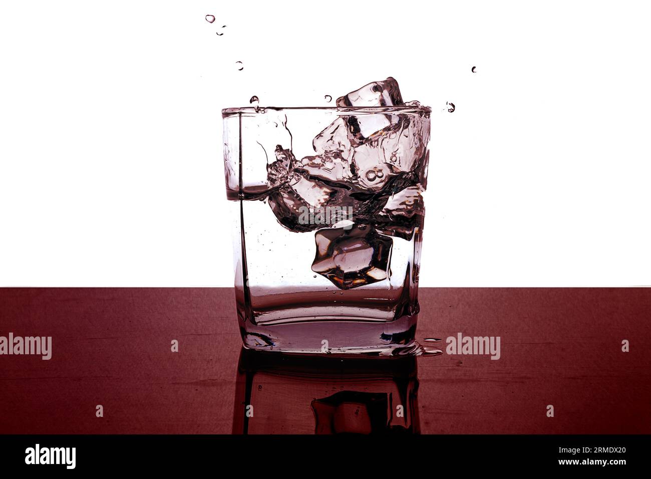 A glass of water, ice cubes and twisted water White and maroon background. Water splash Stock ...