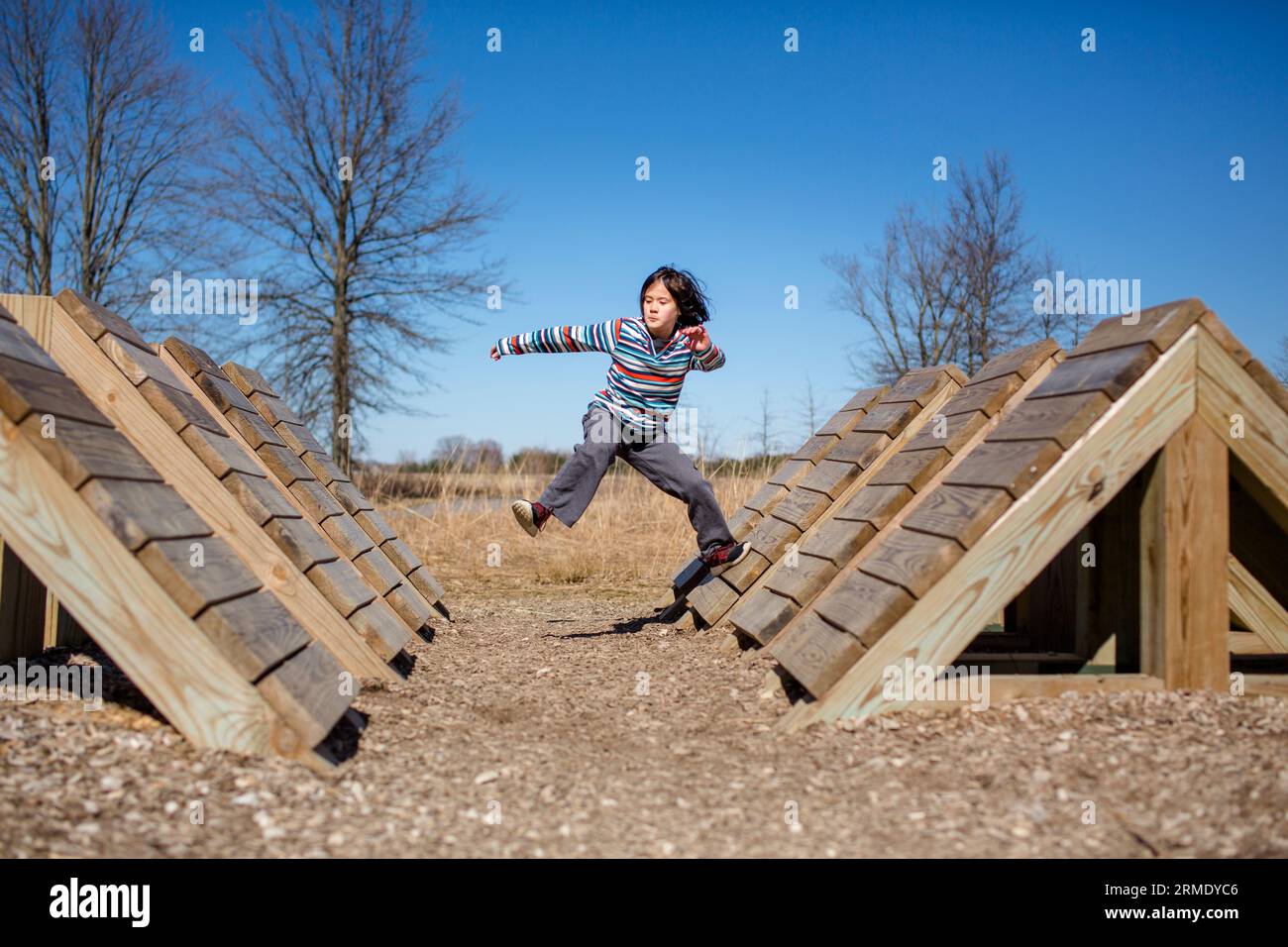 Portrait of a child mid-leap jumping across an obstacle course in park ...