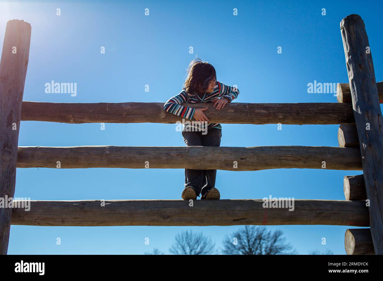 a child climbs on a high wooden fence in sunlight looking over Stock ...
