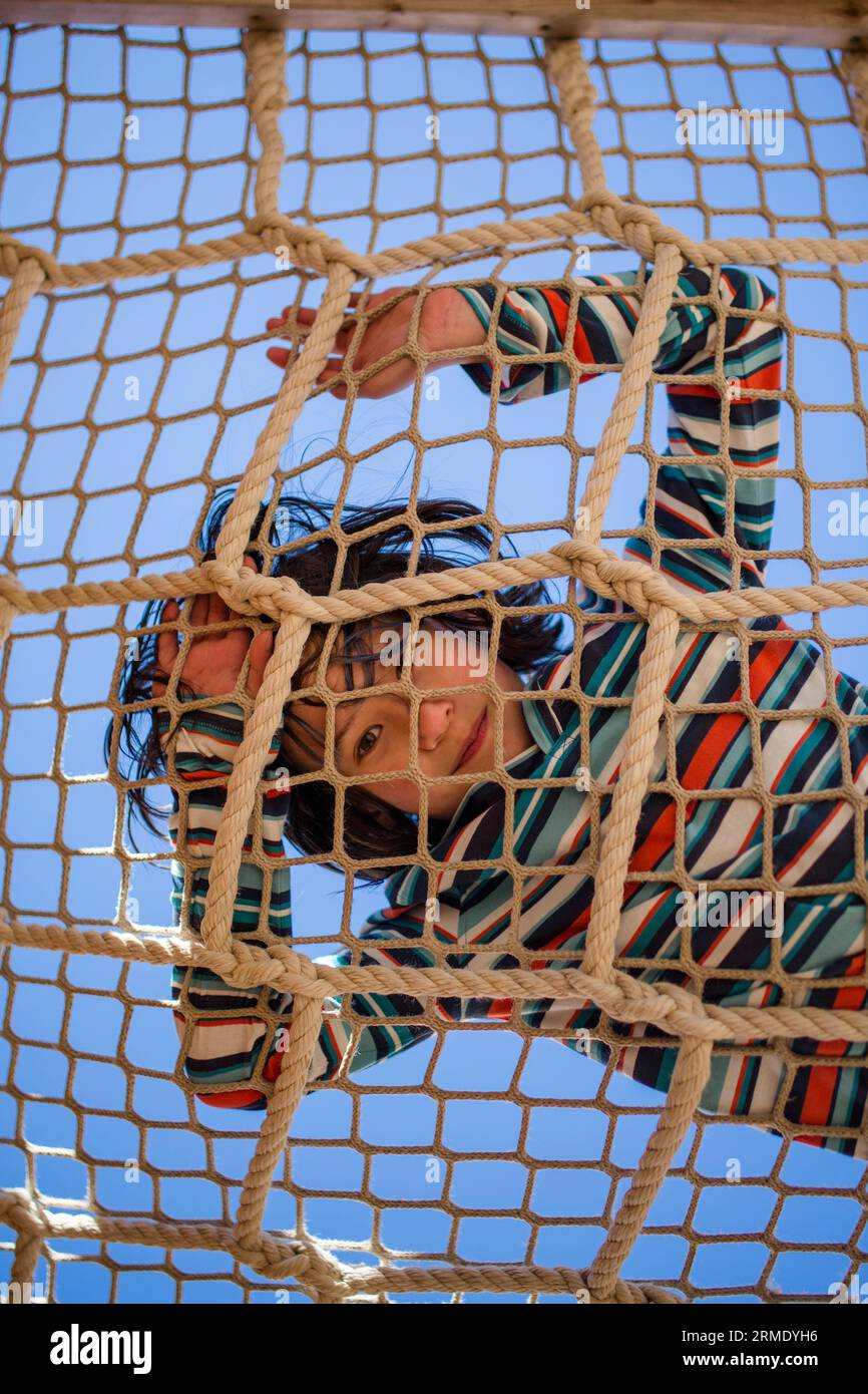 A smiling child looks drown through a rope net against a blue sky Stock ...