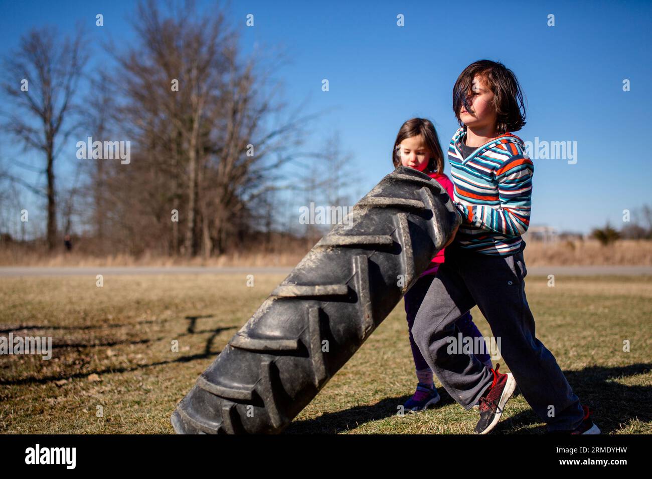 two small children work together to lift a heavy tire in a park Stock ...