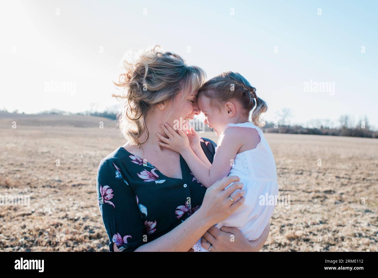 mother and daughter cuddling and laughing whilst standing in a field ...