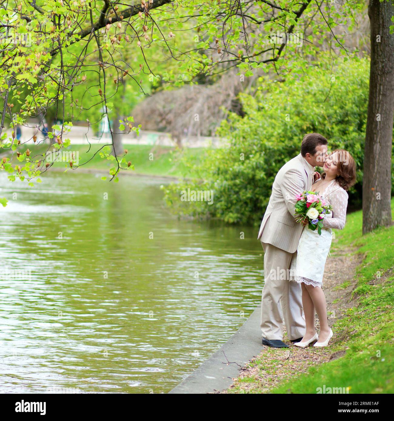 Happy just married couple hugging and kissing near the lake in park ...