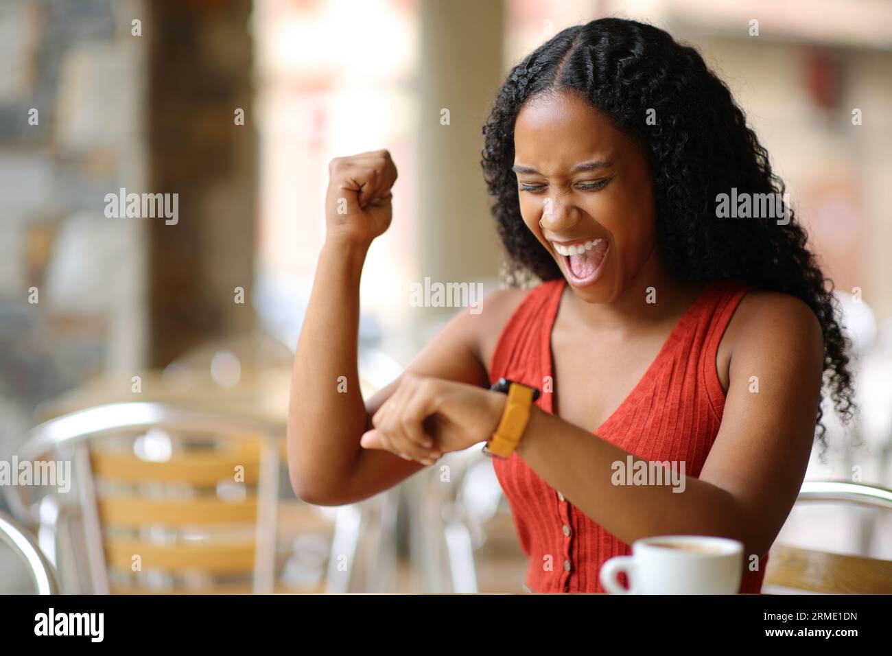 Excited black woman checking smartwatch siting in a bar terrace Stock ...