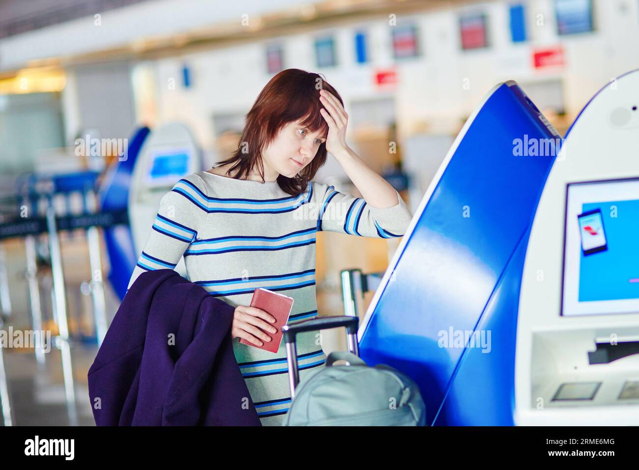 Young female passenger at the airport, doing self check-in, stressed ...