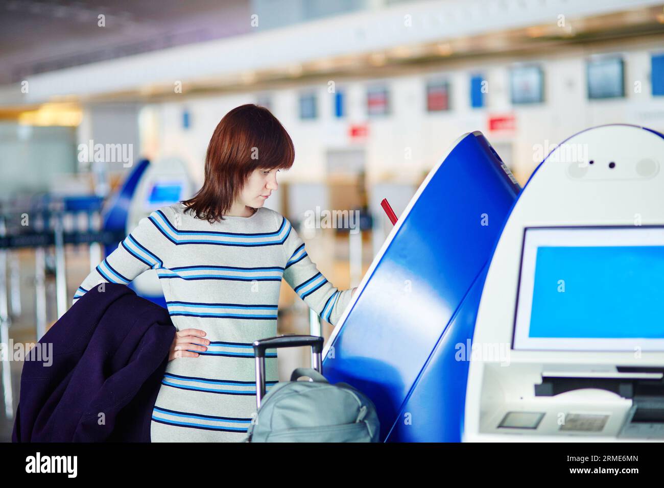 Young female passenger at the airport, doing self check-in at counter ...