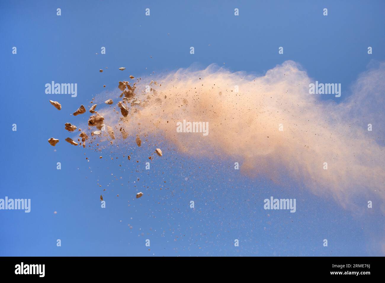 Flying rock debris and dust cloud against blue sky Stock Photo - Alamy