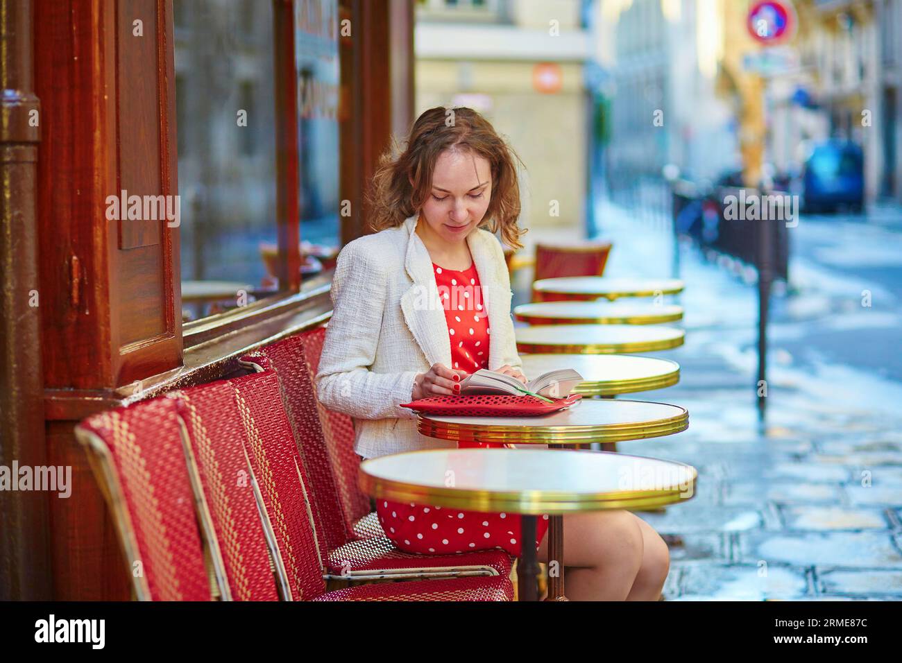 Beautiful young woman in red polka dot dress reading a book or planning ...